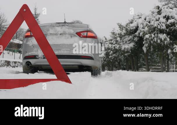 A car is stuck in deep snow along a roadside. A bright red warning ...