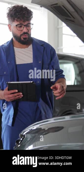 Professional male mechanic in overalls inspecting a car engine with an ...