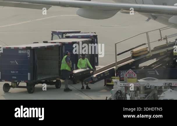 Baggage handlers working on the tarmac, moving suitcases from a ...
