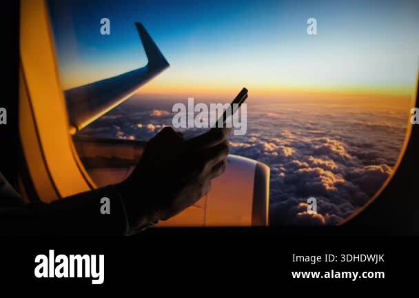 Sunset airplane window view with phone, silhouette of hand scrolling on ...