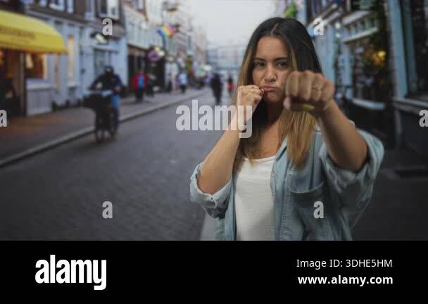 Young hispanic woman punching with fist toward camera in city street ...