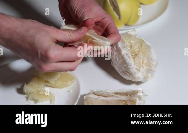 Close up of hands peeling a pomelo segment with an orange tool on a ...
