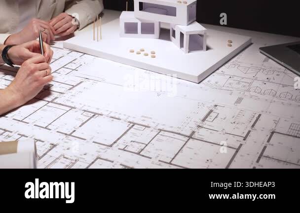 Architects collaborating over blueprints and scale model, measuring and ...