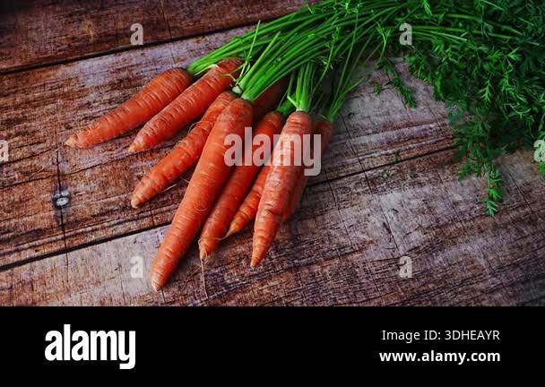 Fresh raw carrots with leafy green tops arranged on wooden table ...