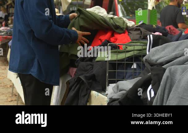 Soft daylight over piles of used clothes while a man examines garments ...