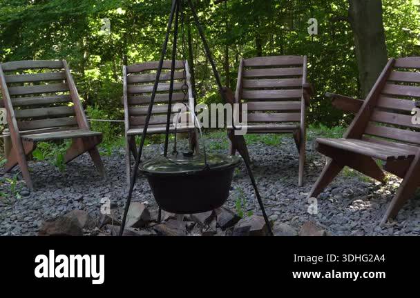 People gather around a fire pit in the woods. They prepare to cook food ...