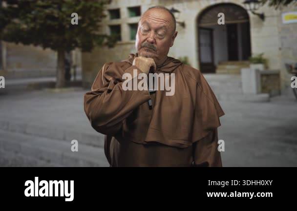 Man monk with hand on chin, eyes closed, standing before a stone church ...