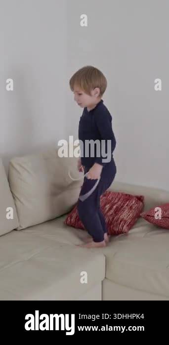 Happy child wearing pajamas is jumping and playing on a white sofa with ...