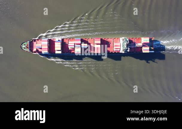 A massive cargo ship steams steadily out of the harbor, its hull ...