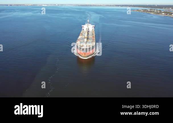 A massive cargo ship steams steadily out of the harbor, its hull ...