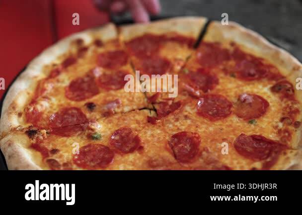 A hand takes a slice of pepperoni pizza, showcasing gooey cheese and a ...