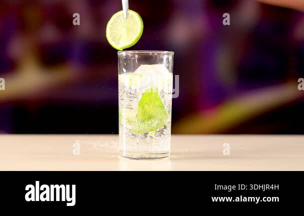 A lime slice is added to a mojito cocktail in a vibrant bar setting ...