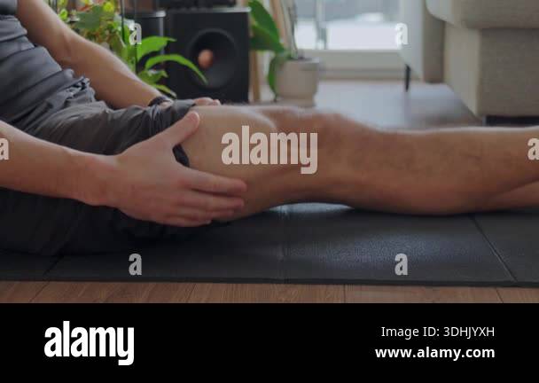 Man holding leg muscle while sitting on fitness mat indoors at home ...