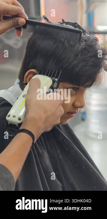 Young boy getting a professional haircut at a salon, as a barber uses ...