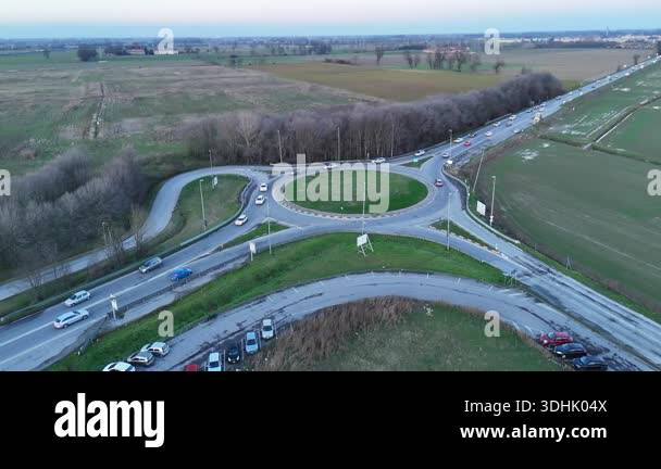 Cars navigate a multi-lane roundabout with surrounding roads and fields ...