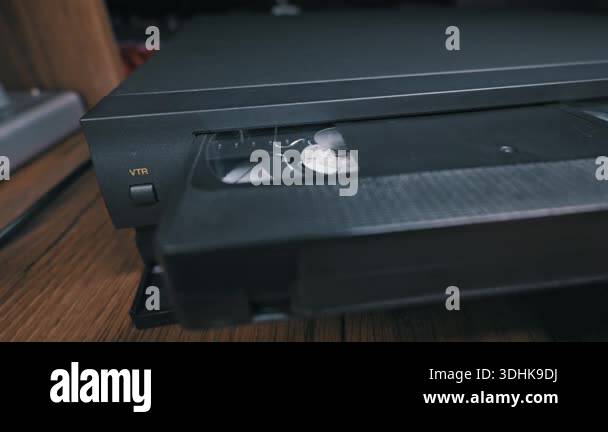 Male hand inserts black VHS cassette into motorized slot of vintage VCR ...