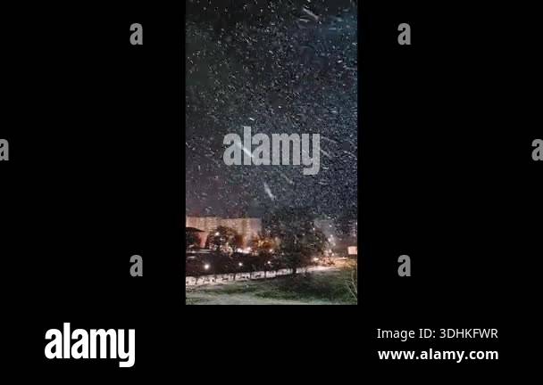 Nighttime urban scene with snow falling through a bright streetlight ...