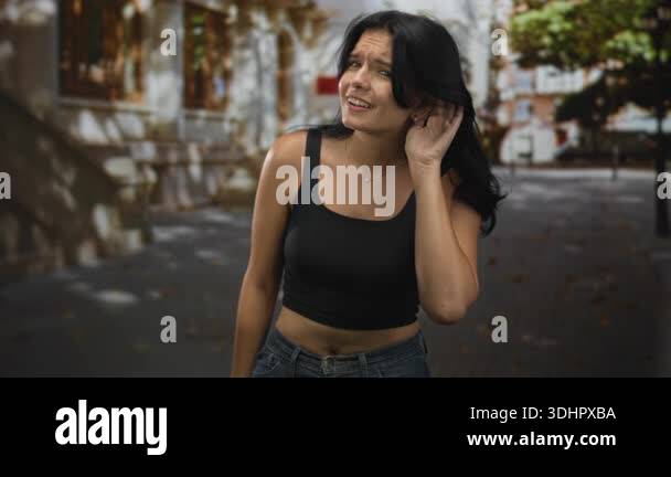 Young hispanic woman holds hand to ear listening gesture while leaning ...