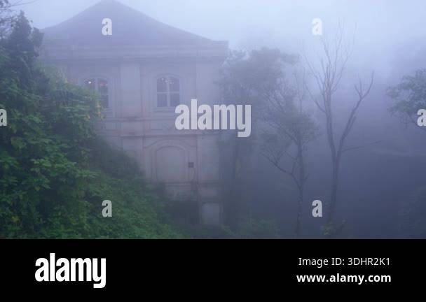 Old stone Building partially hidden by thick Fog with dimly lit Windows ...