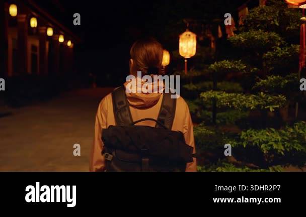 Traveler Standing Near Lantern Lit Path at Night with Warm Glow and Medium Angle expressing ...