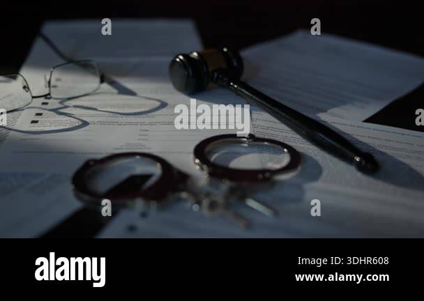 A judge gavel, handcuffs, and eyeglasses rest on legal documents under ...