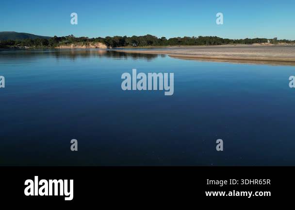 Peaceful aerial view of a wide, calm river with a sandy bank and lush ...