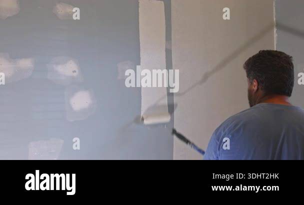 Handy man paints wall using roller wall has patches fresh layer of ...