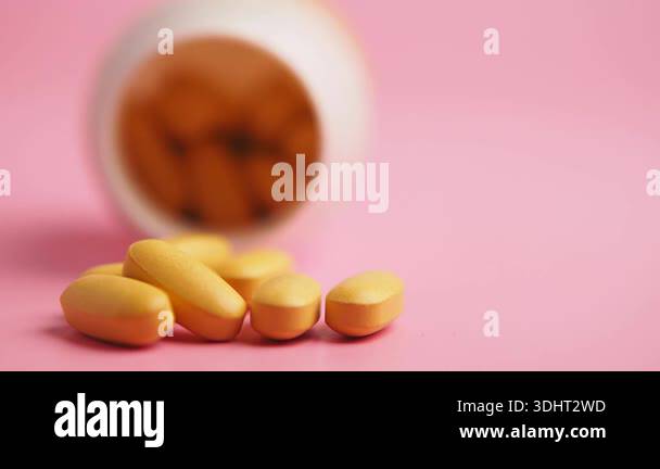 yellow color vitamin Pills spill from a container on a pink color ...