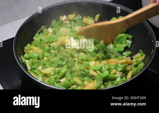 Chopped green bell peppers and onions are cooked in a frying pan Stock ...