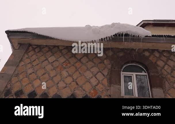 Massive ice and snow hanging from a building roof during heavy snowfall ...