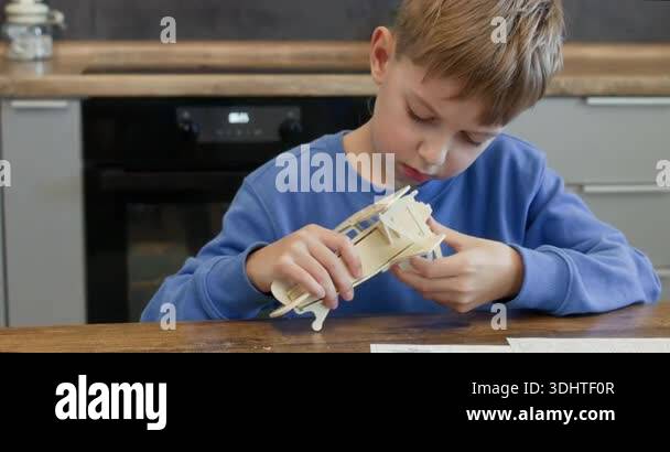 Junior schoolboy observes vintage airplane model made of wooden details ...