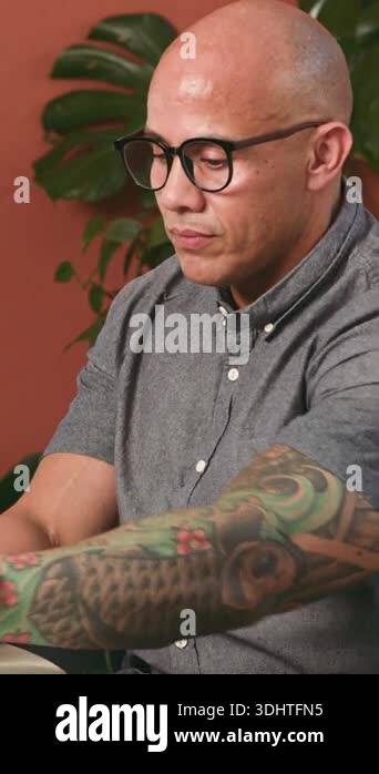 Concentrated bald man with stylish glasses and arm tattoos diligently ...