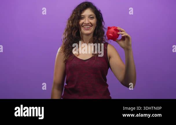 Woman holding red piggy bank and extending hand toward camera in purple ...