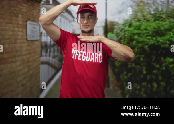 Man lifeguard in red shirt and cap frames face with hands and visible ...