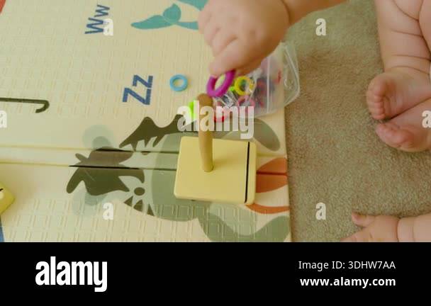 A young child skillfully stacks rings on a post while reaching for ...