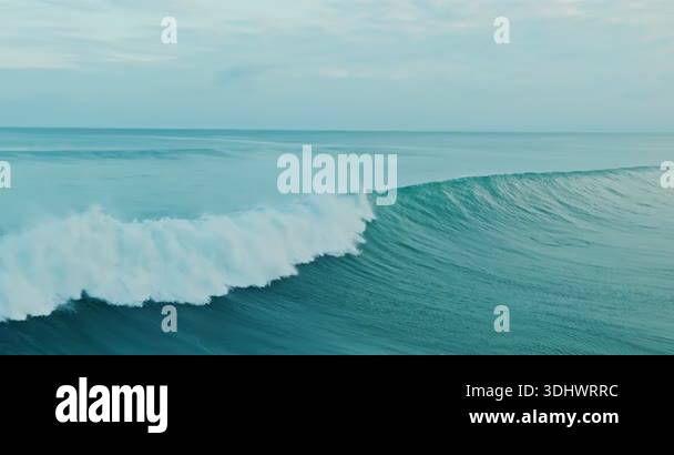 Aerial slow motion shot of a powerful ocean wave rolling across calm ...