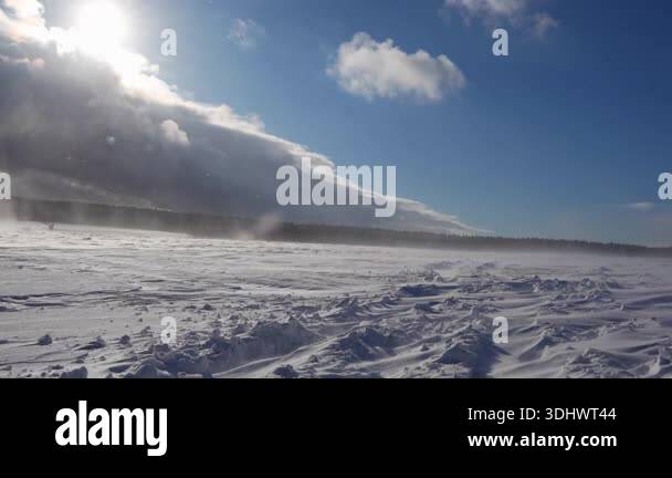 A vast snowy field experiences powerful winds, causing snow to swirl ...