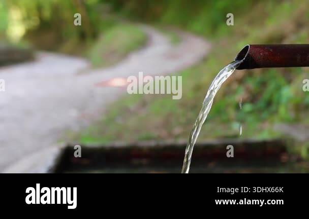 Close up of fresh, clean spring water flowing from a rustic metal pipe ...