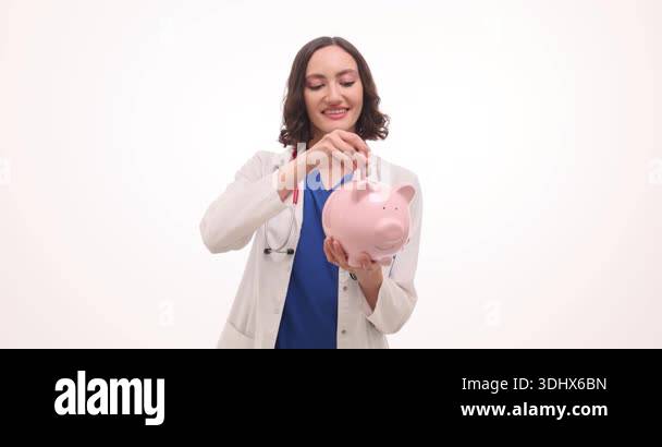 Smiling woman doctor in uniform holds pink piggy bank laughing. Medical ...