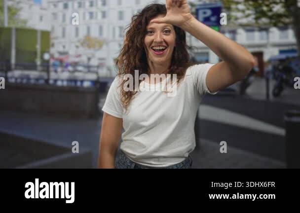 Woman shows tongue and makes l with hand to forehead on urban street ...