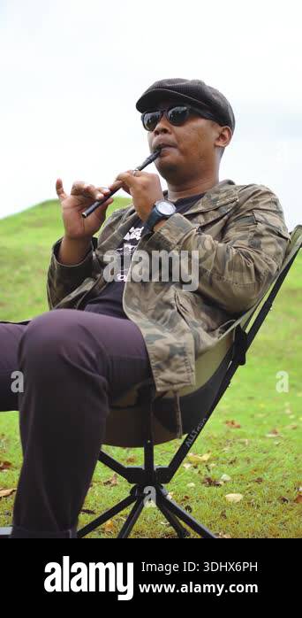 A male musician sits on a portable chair and play a tin whistle in a ...
