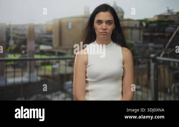 Woman wearing white tank top frowning with pouted lips and hollow gaze ...