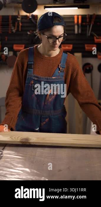 Female carpenter or joiner in overalls stacking wooden boards on table ...