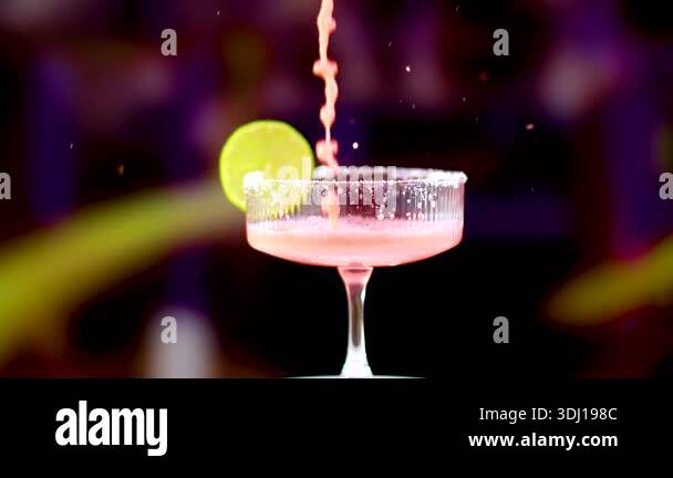 A pink margarita is poured into a glass, garnished with a lime slice ...