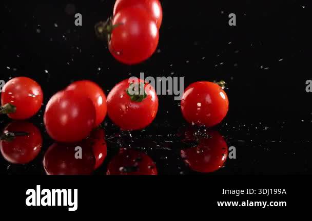Cherry tomatoes drop onto a reflective black surface, creating splashes ...