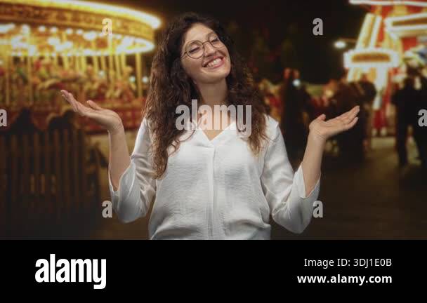 Woman waving hands at street fair at night, smiling with hands on hips ...