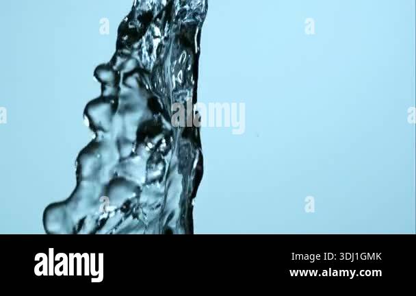 A thick stream of clear water falling down vertically against a light ...