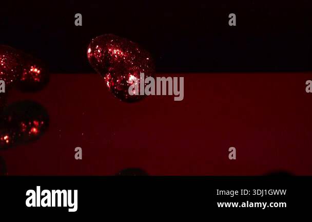 Red glittery hearts falling and bouncing on a red reflective surface ...