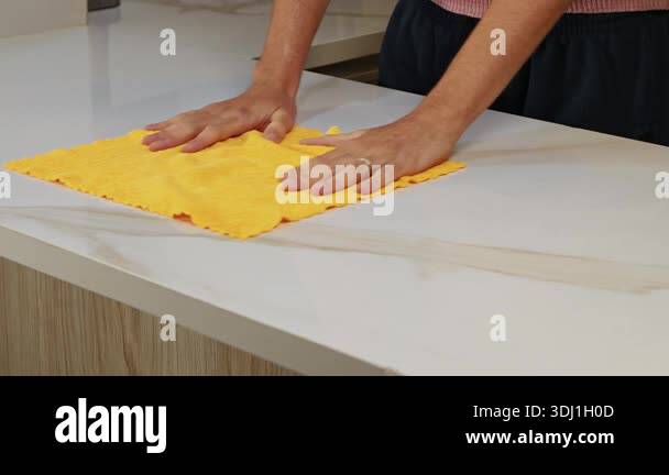 Young woman wiping a modern kitchen countertop with a cleaning cloth ...