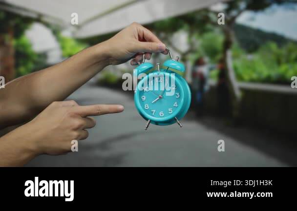 Man holding blue clock with finger pointing at time outdoors in park ...
